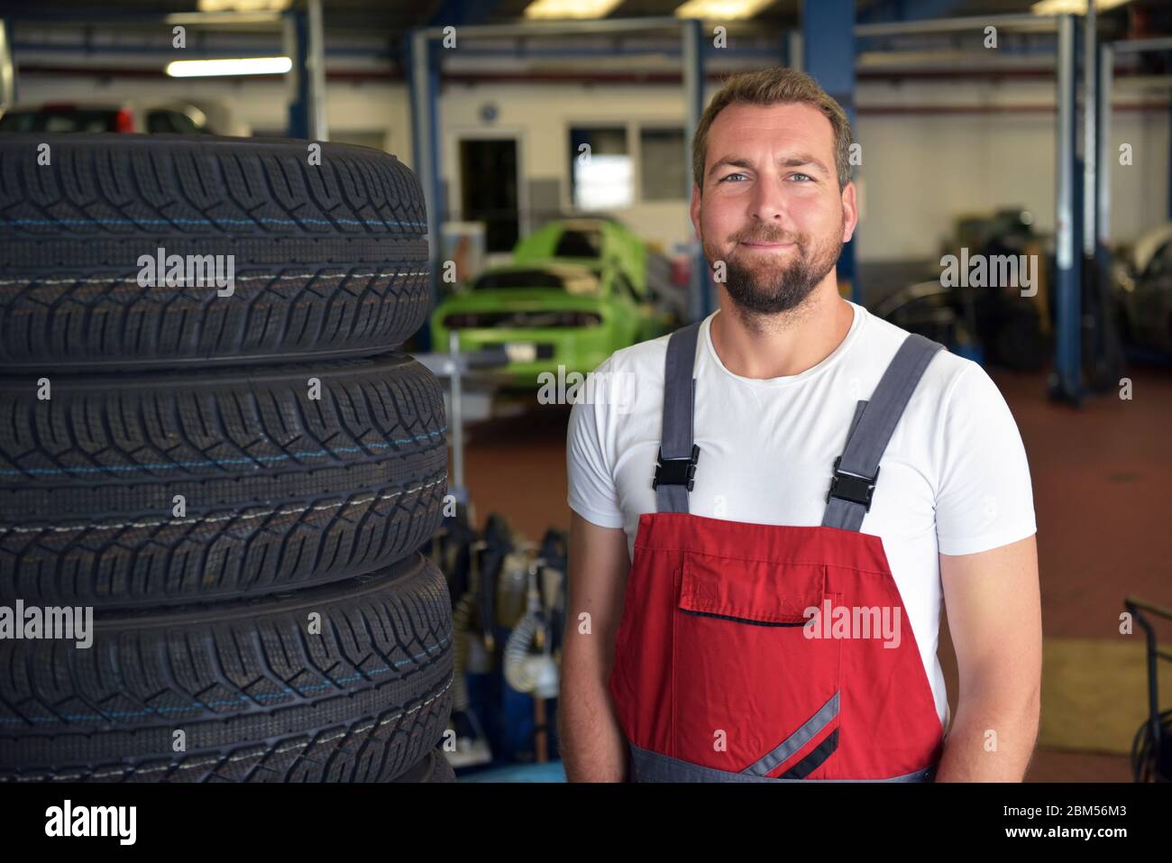 Portrait of successful smiling car mechanic in a workshop on a stack of ...