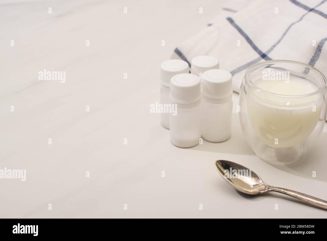 Glass of homemade yogurt near teaspoon, containers with starter ...