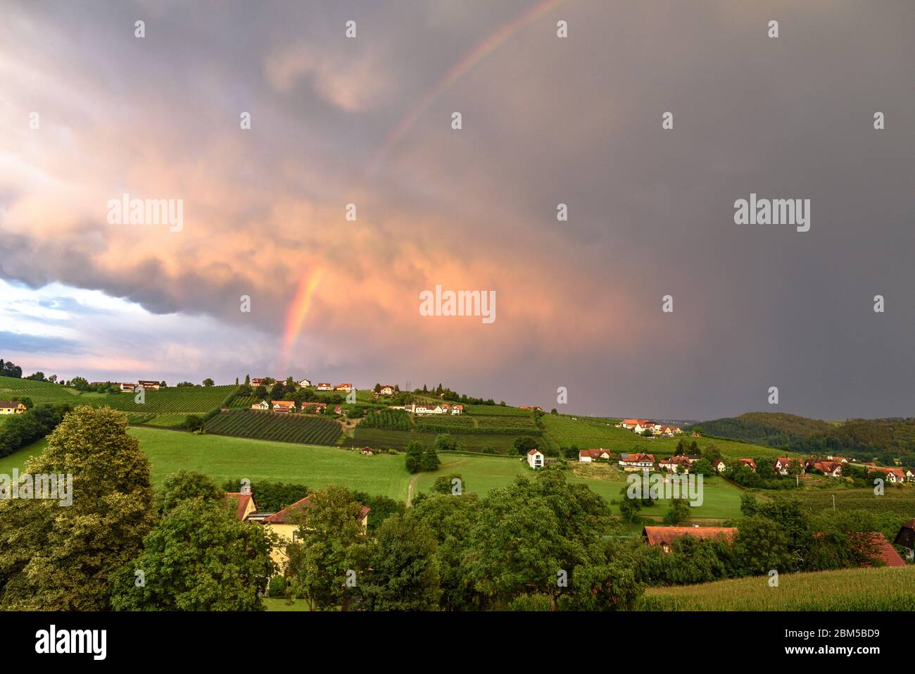 A rainbow visible above houses on a hillside in Riegersburg, Austria ...