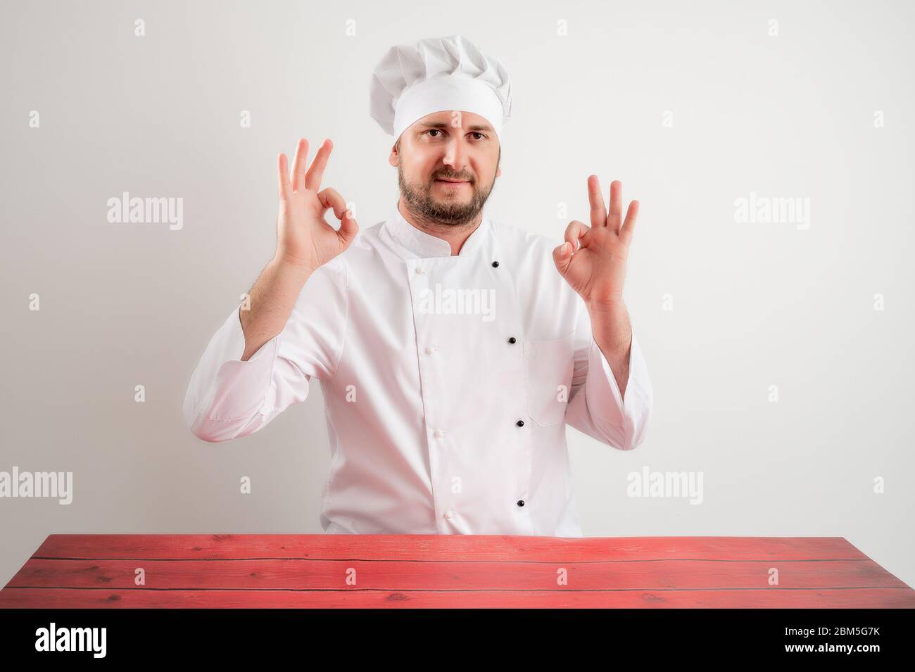 Young male chef in white uniform showing double OK sign posing on a ...