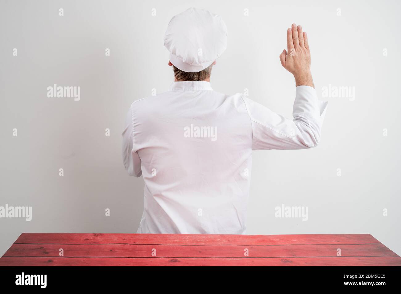 Young male chef in white uniform showing oath from behind posing on a ...