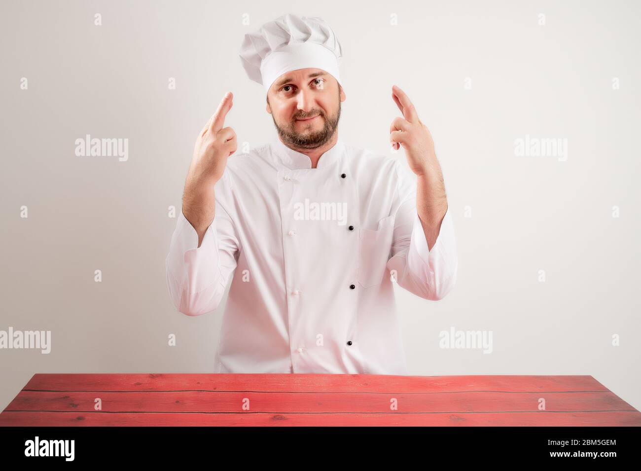 Young male chef in white uniform showing double good luck posing on a ...
