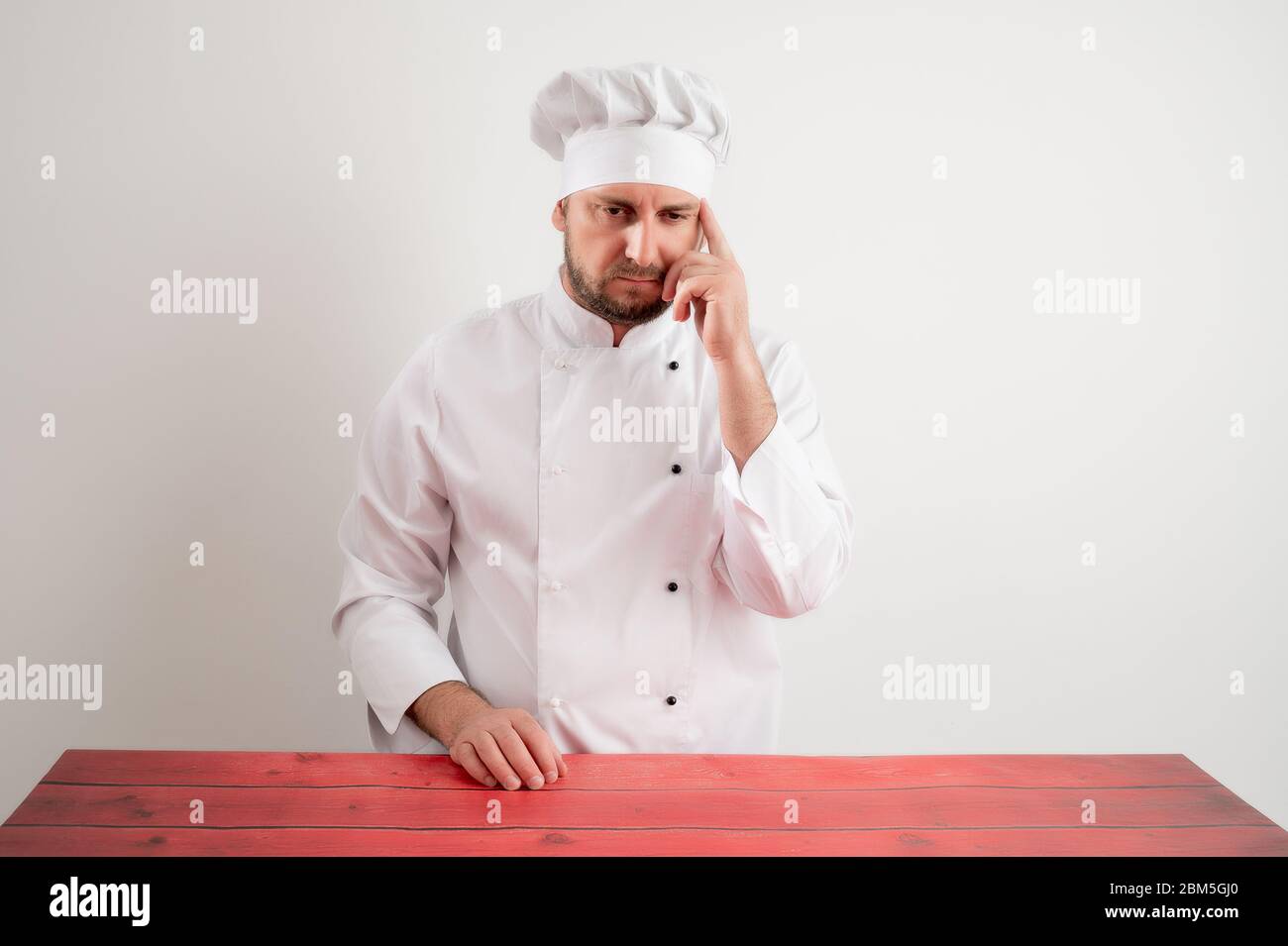 Young male chef in white uniform wondering posing on a white isolated ...