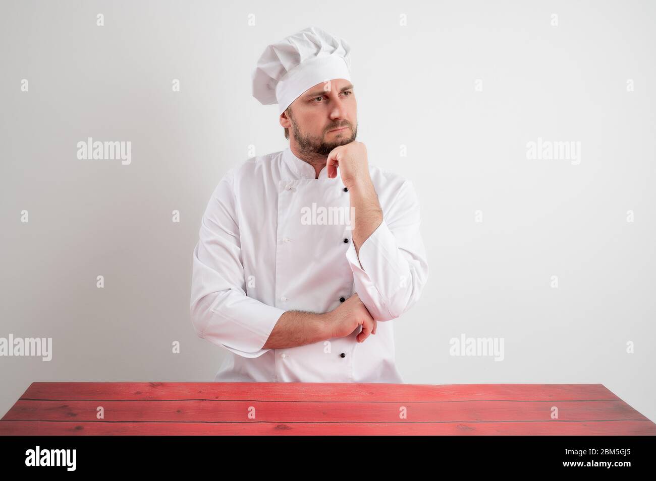 Young male chef in white uniform holding hand under her chin, having ...