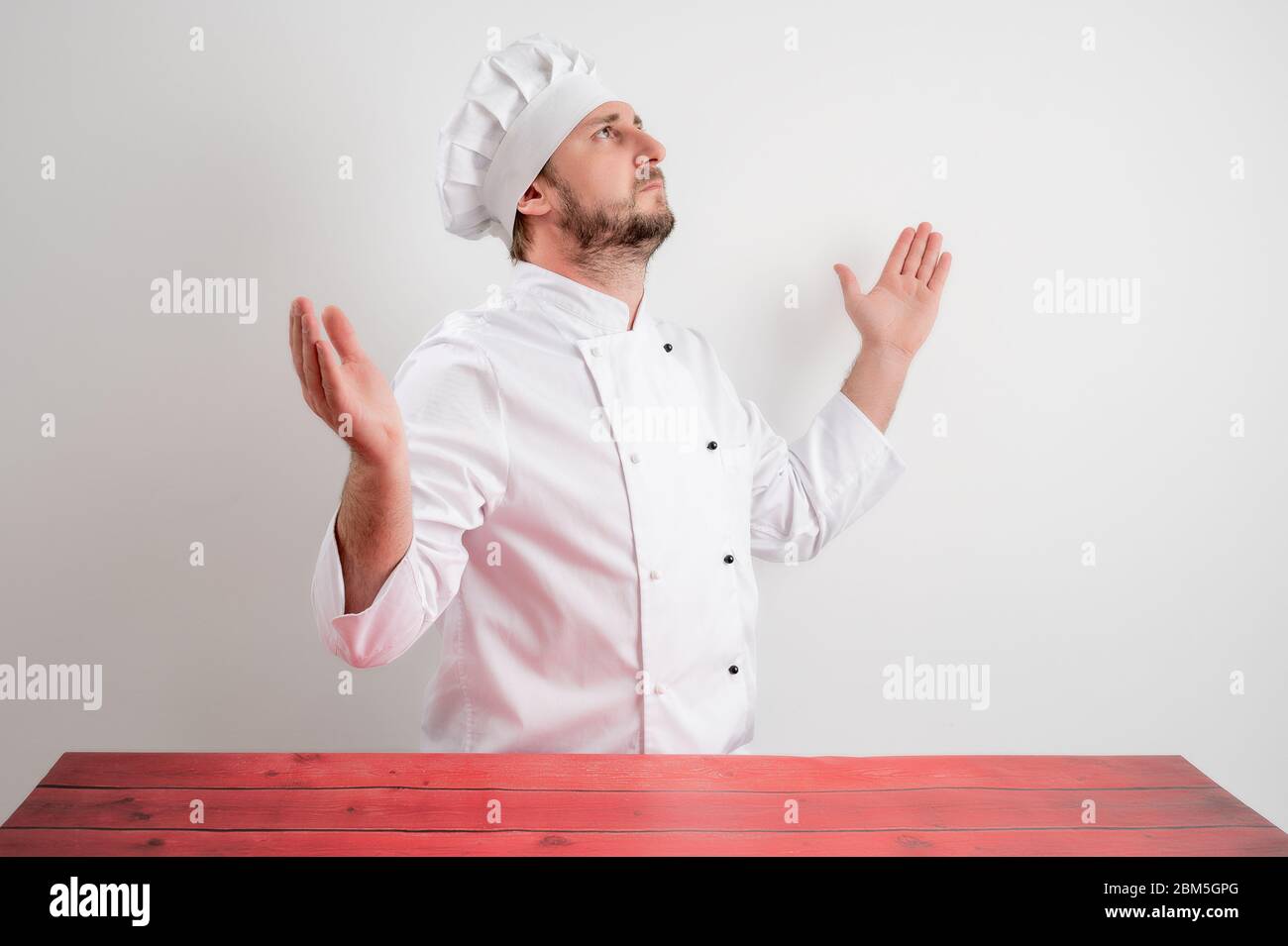 Portrait of young male chef in white uniform with open arms looking up ...