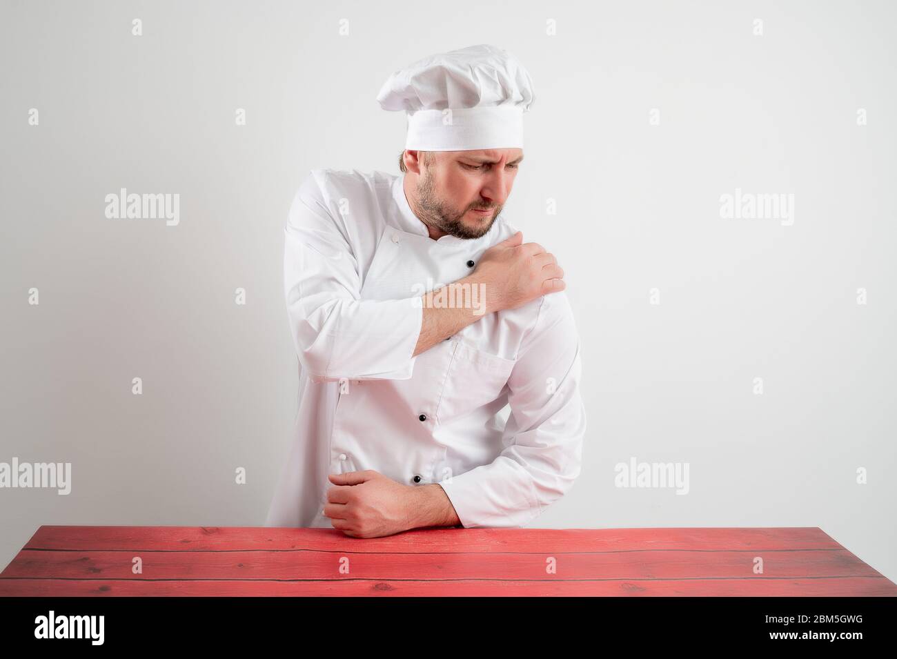 Young male chef in white uniform has shoulder pain posing on a white ...
