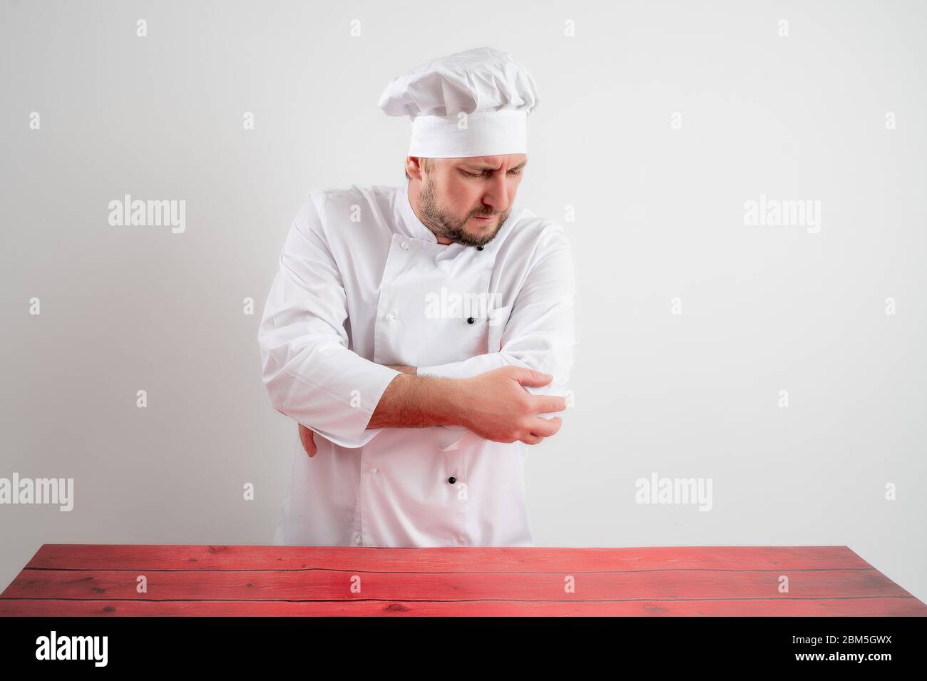 Young male chef in white uniform elbow pain posing on a white isolated ...