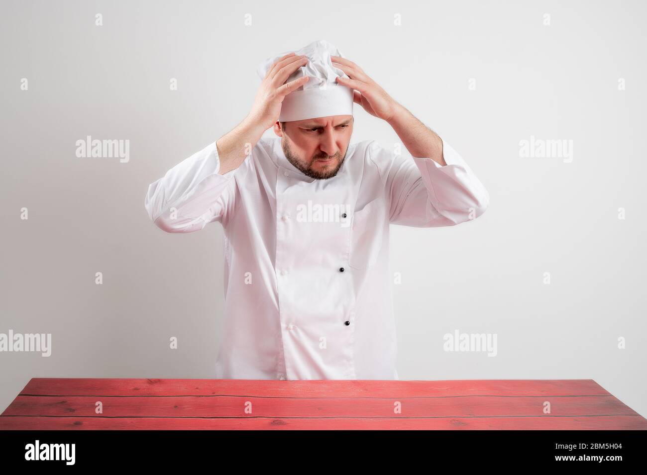 Portrait of young male chef in white uniform with open arms looking up ...