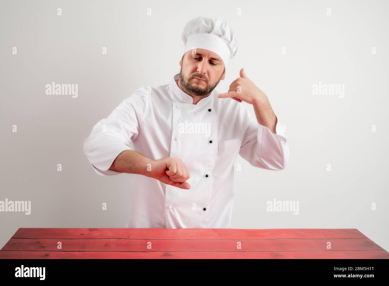 Portrait of young male chef in white uniform showing call me gesture ...