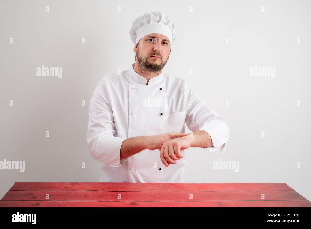 Portrait of young male chef in white uniform showing it's time gesture ...