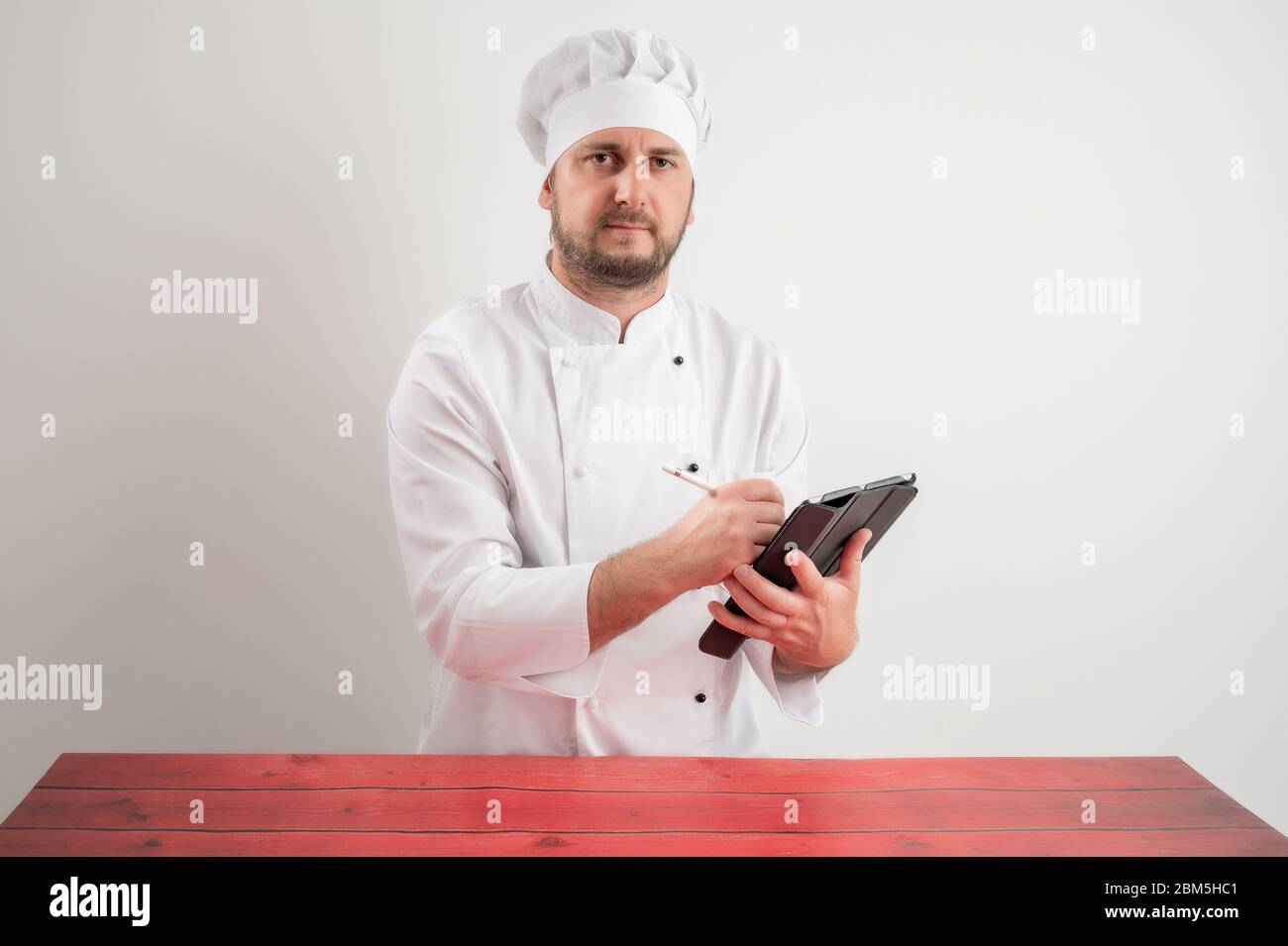 Portrait of young male chef in white uniform takes notes, looking at ...