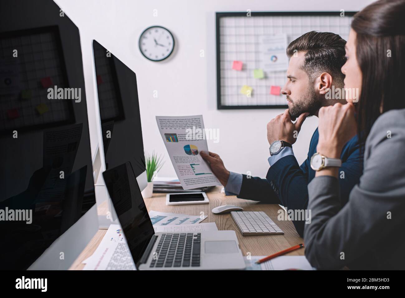 Side view of computer systems analysts working with charts near computer monitors with blank ...