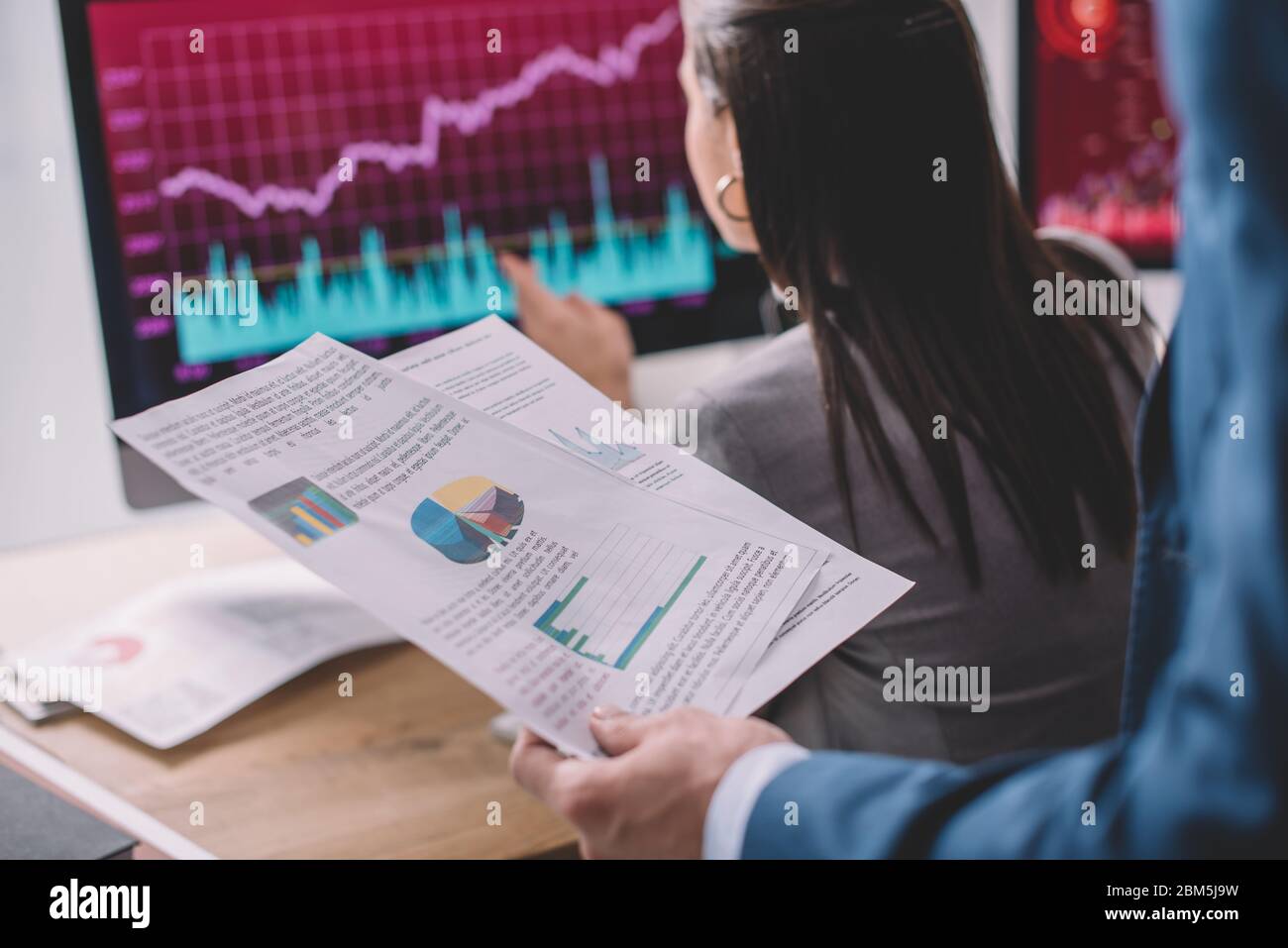 Selective focus of data analyst holding papers with graphs near colleague working with computers ...