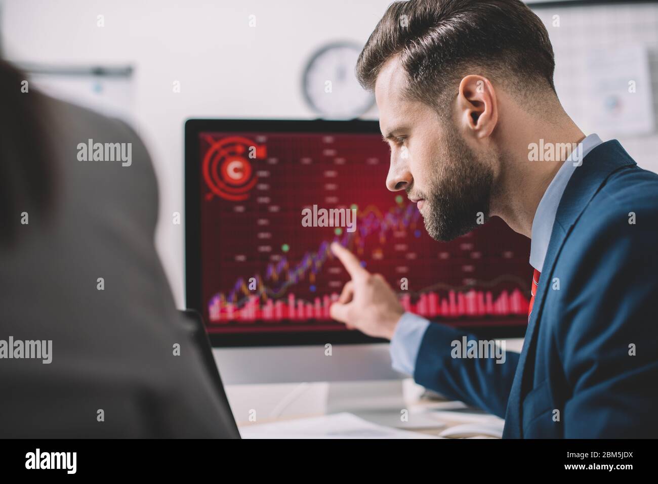 Selective focus of analyst pointing on charts on computer monitor while working with colleague ...