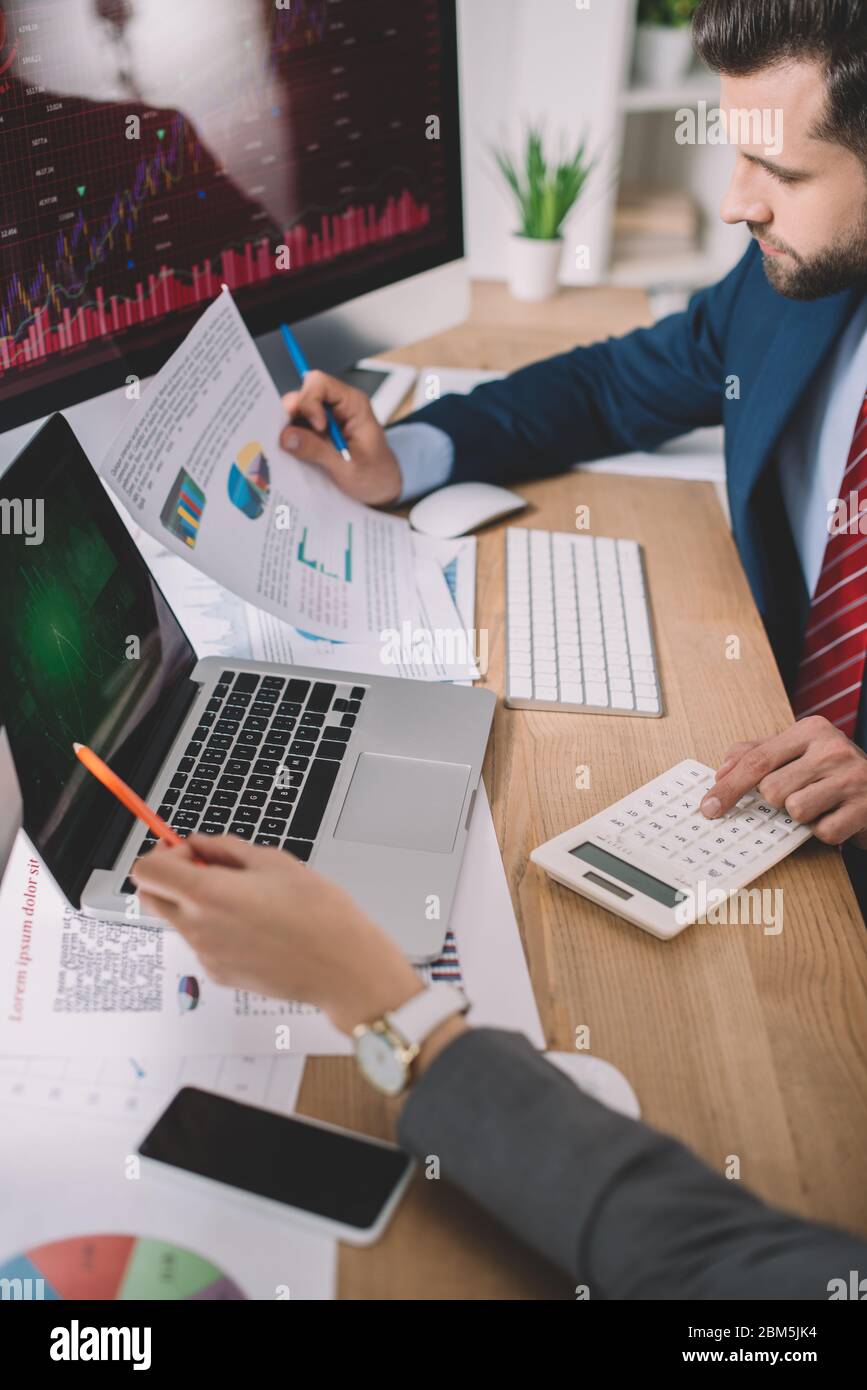 Selective focus of data analyst working with charts and calculator near colleague pointing on ...