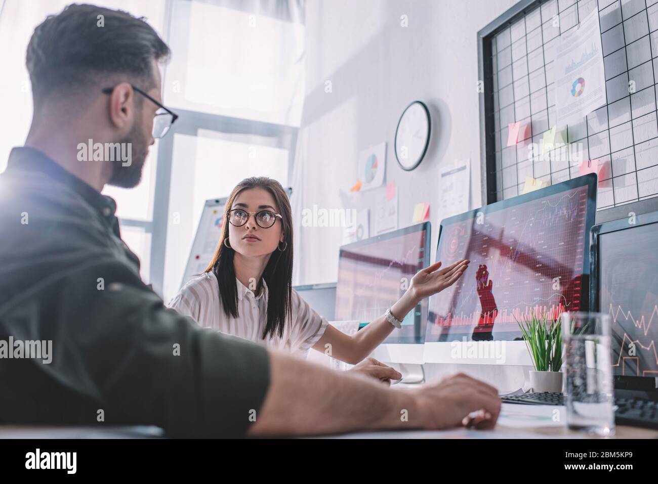 Selective focus of data analyst pointing with hand on computer monitor to colleague in office ...