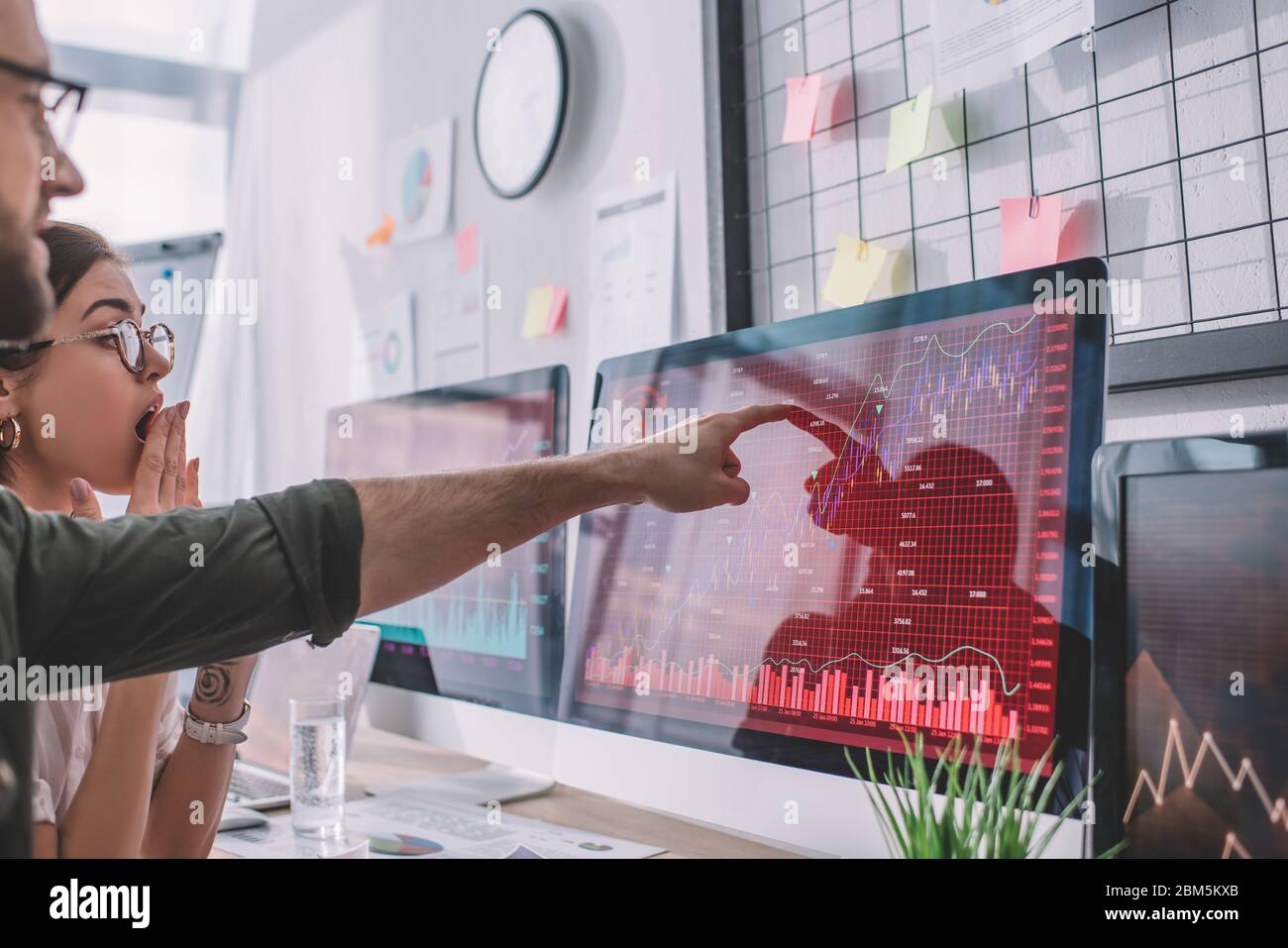 Selective focus of data analyst pointing on charts on computer monitor at shocked colleague ...