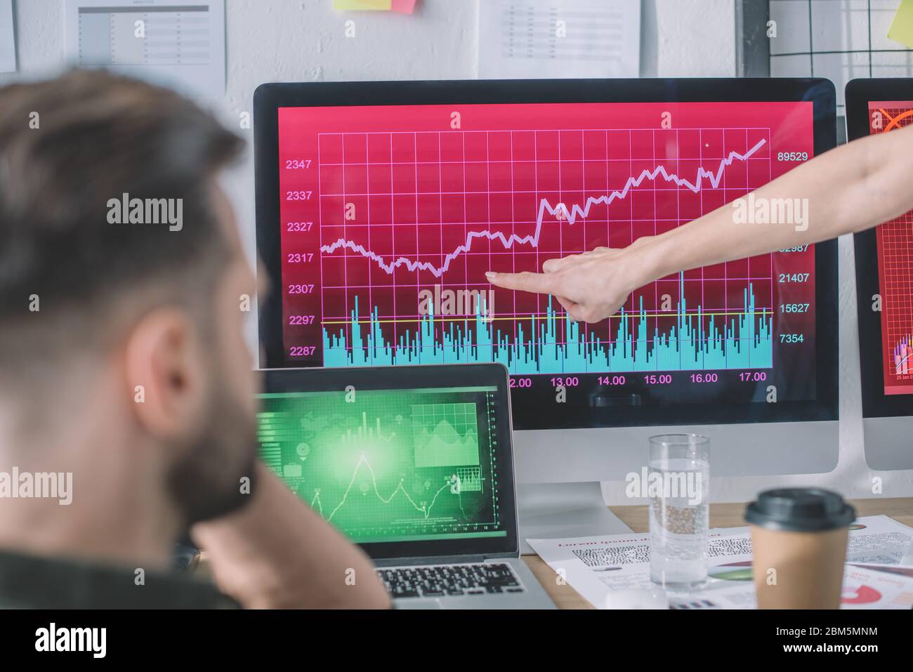 Selective focus of data analyst pointing at chart on computer monitor to colleague in office ...