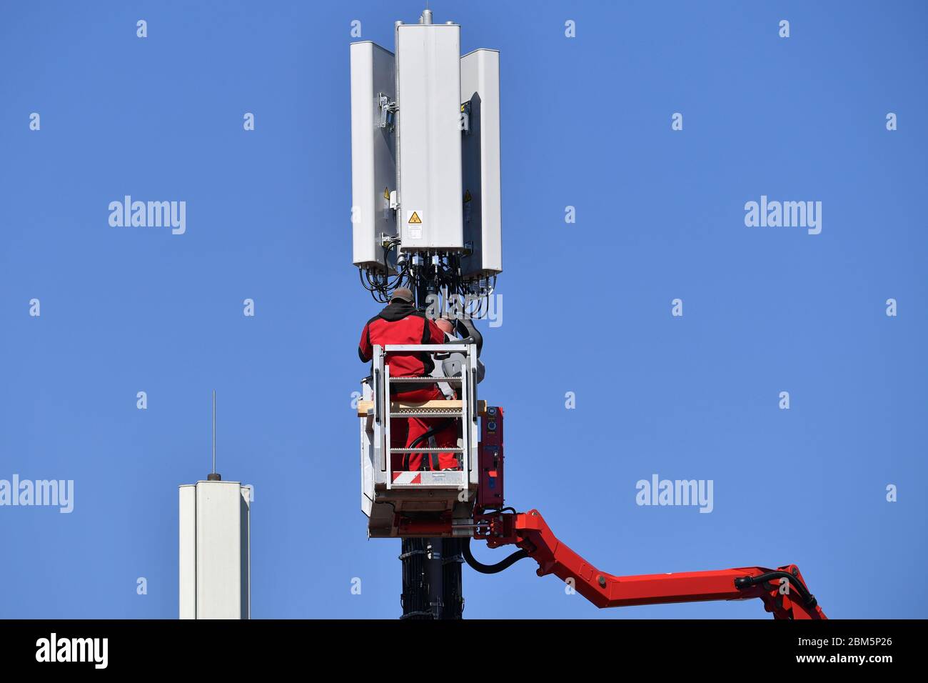 Cell phone mast on a house roof. Workers stand on a lifting platform ...