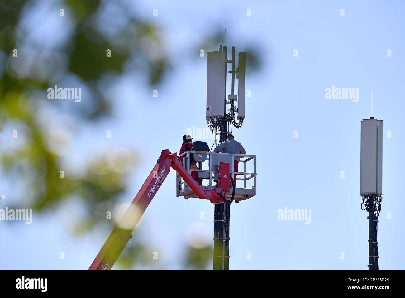Cell phone mast on a house roof. Workers stand on a lifting platform ...