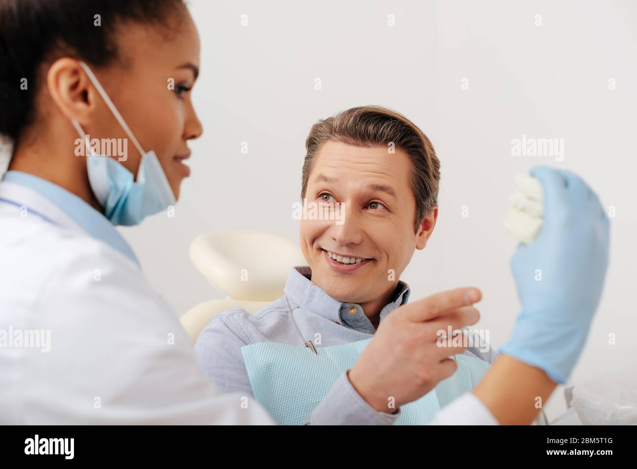 selective focus of happy patient pointing with finger at teeth model ...
