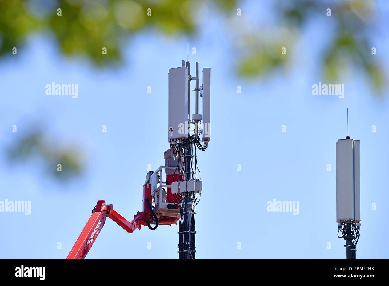 Cell phone mast on a house roof. Workers stand on a lifting platform ...