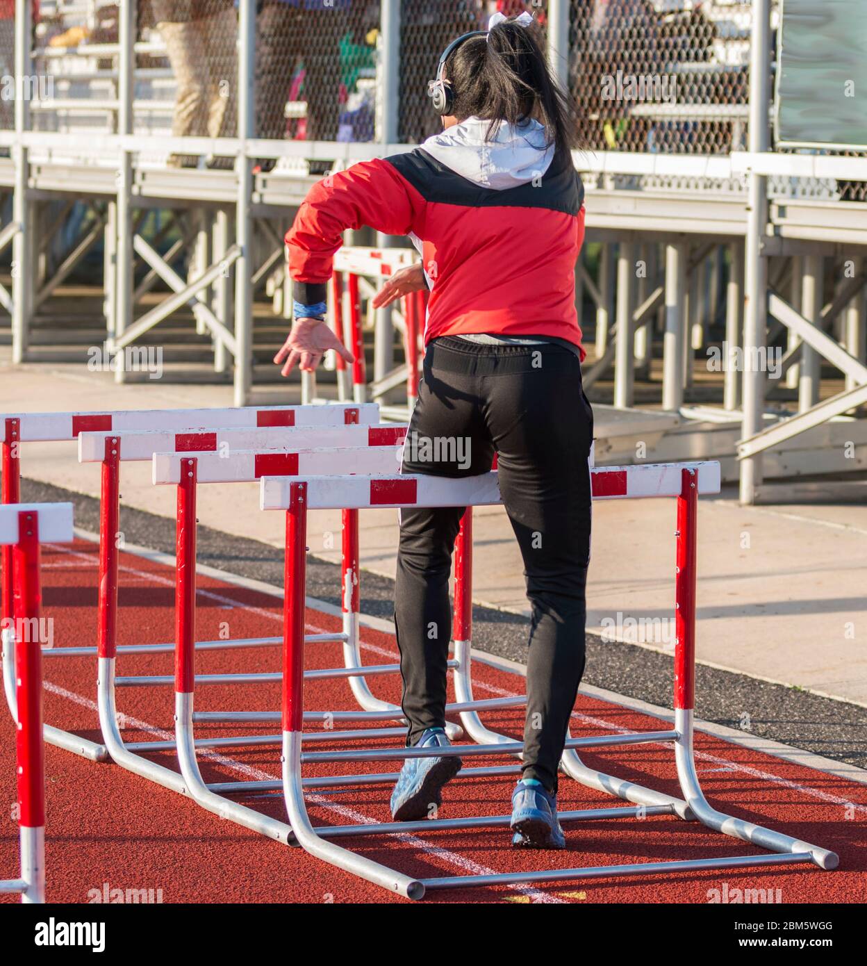 A high school girl os warming up for a hurdle race by performing hurdle ...