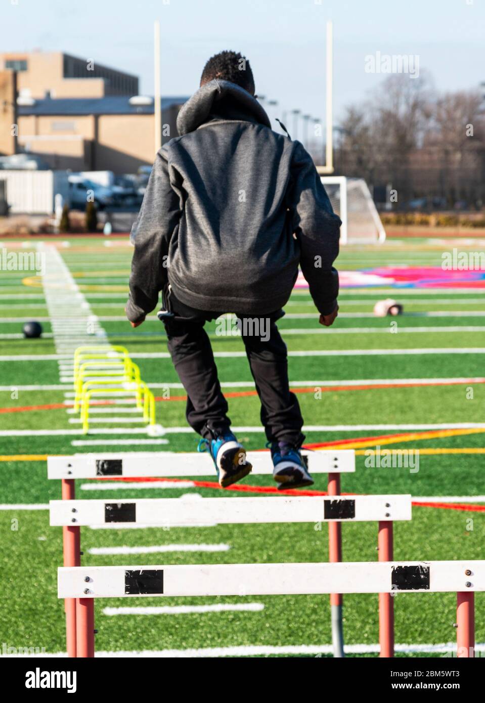 A high school boy is jumping over track hurdles with yellow mini ...