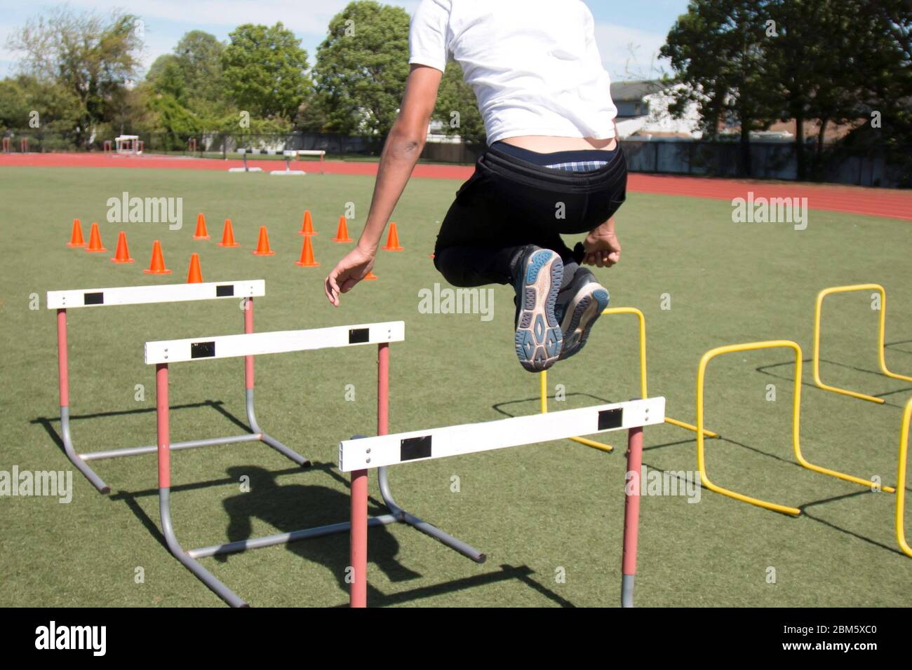 A high school male athlete bounding and jumping over hurdles and orange ...