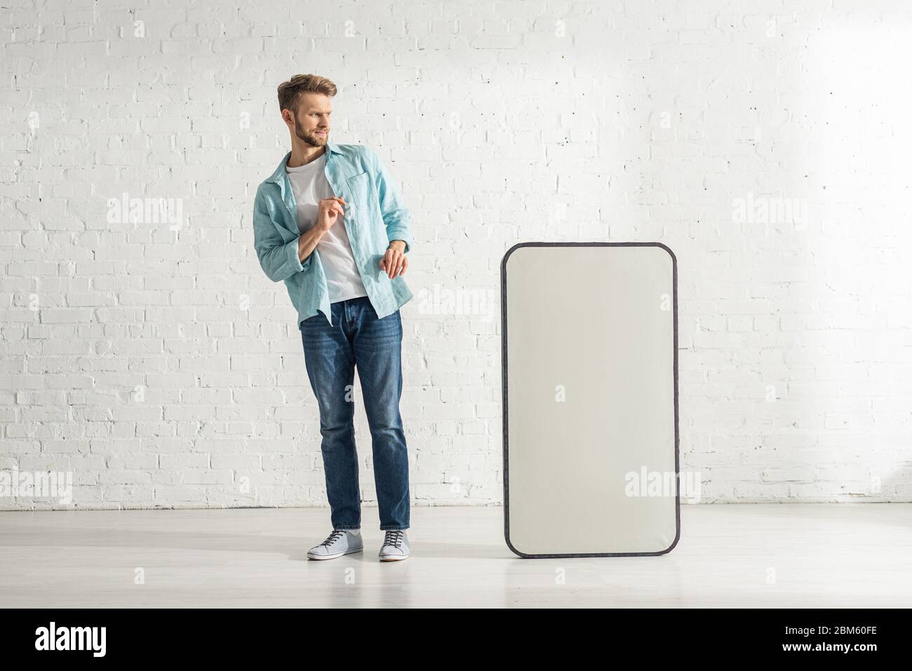 Scared man looking at big model of smartphone near white brick wall ...