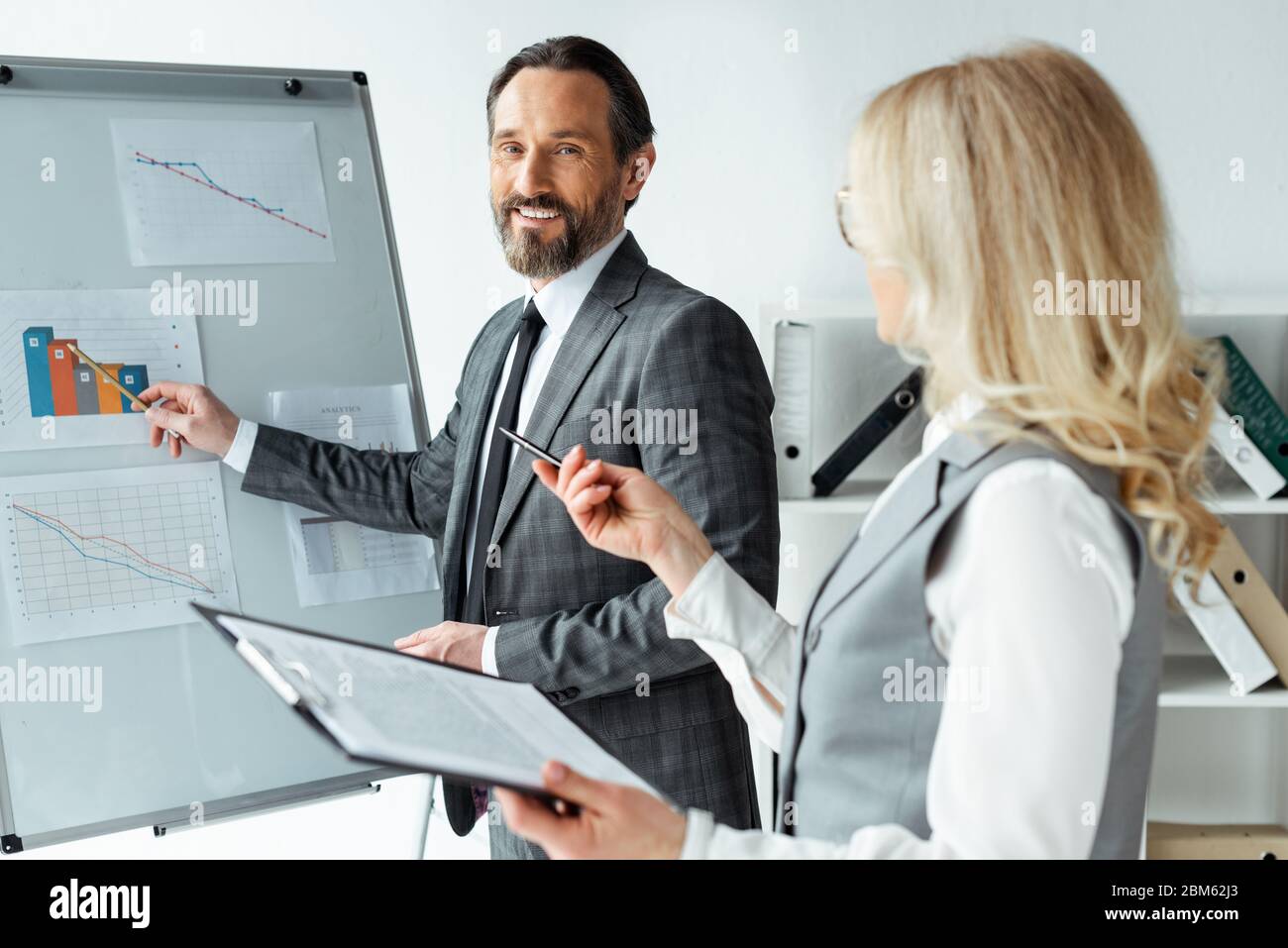 Selective focus of smiling businessman pointing on charts on whiteboard near businesswoman ...
