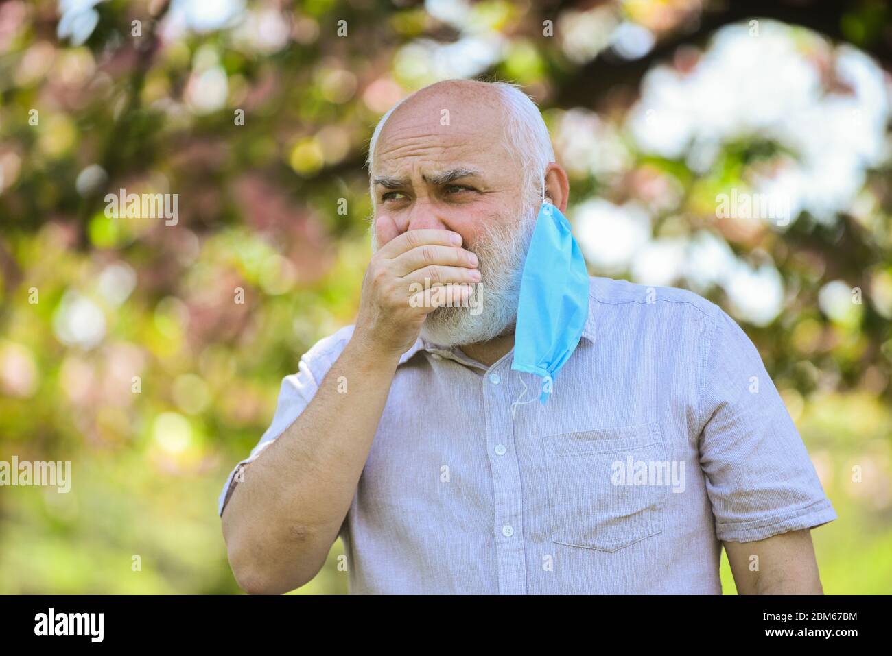 coughing senior man in medical mask. blossom tree in park. life during ...