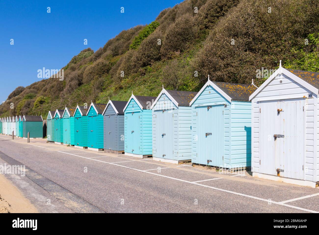 Row of colourful beach huts in shades of green with blue sky on warm ...
