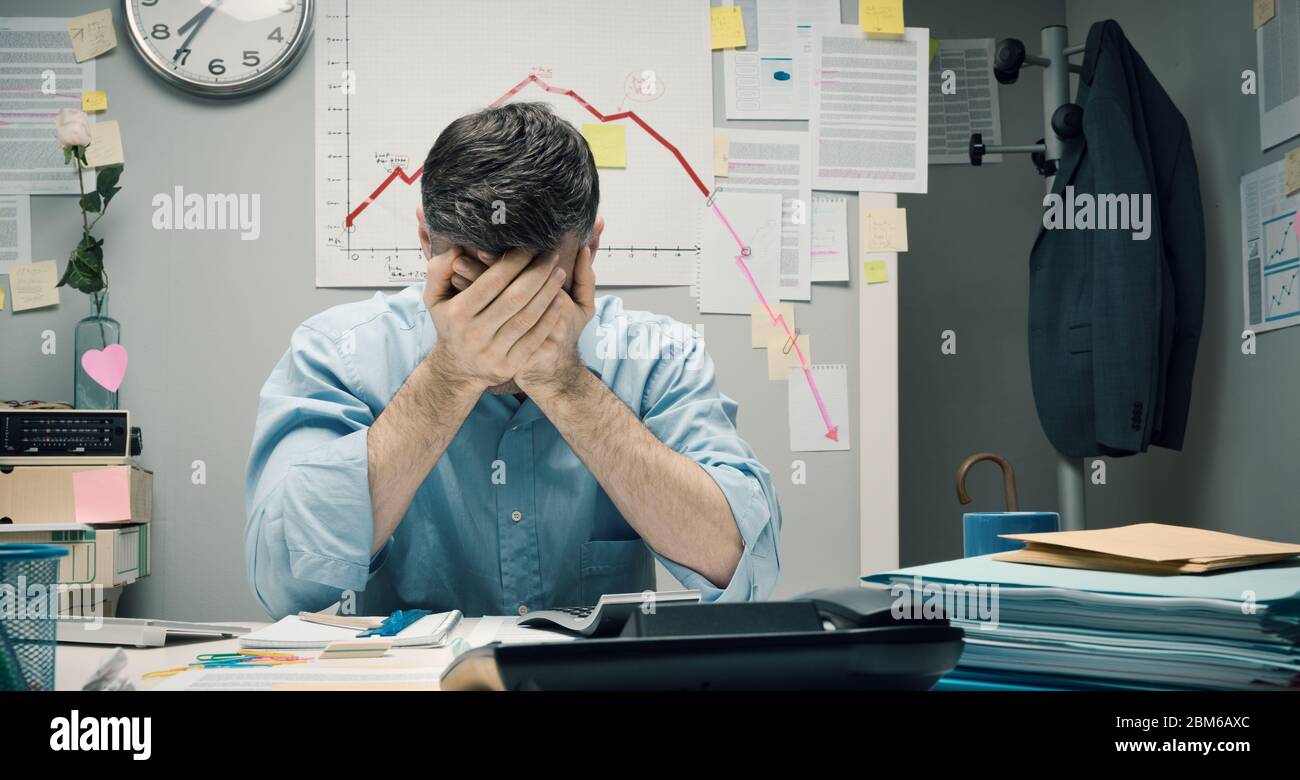 Desperate office worker with head in hands and negative financial chart ...