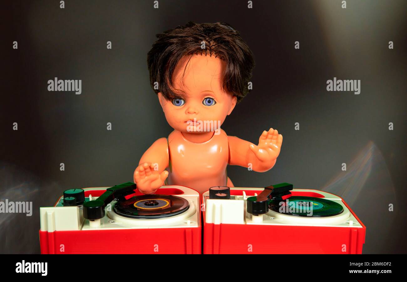 Toy plastic doll DJ playing vinyl on the decks with dark background ...