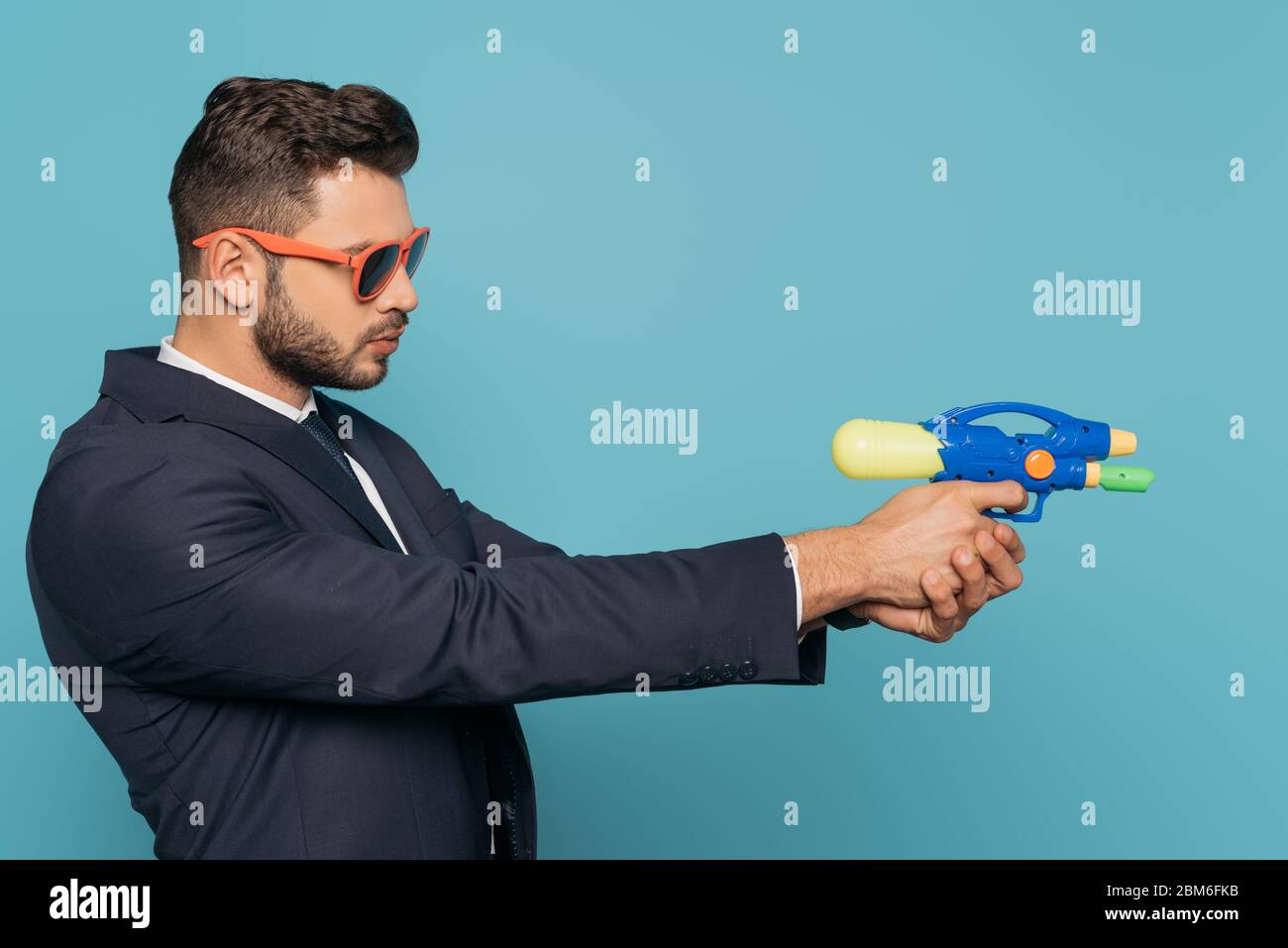 side view of businessman in sunglasses holding toy water gun isolated ...
