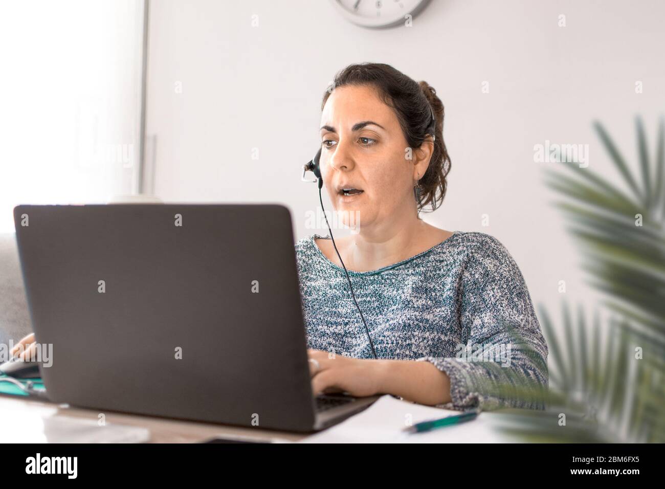 Teleworking woman with a headphones and a laptop computer at home in ...