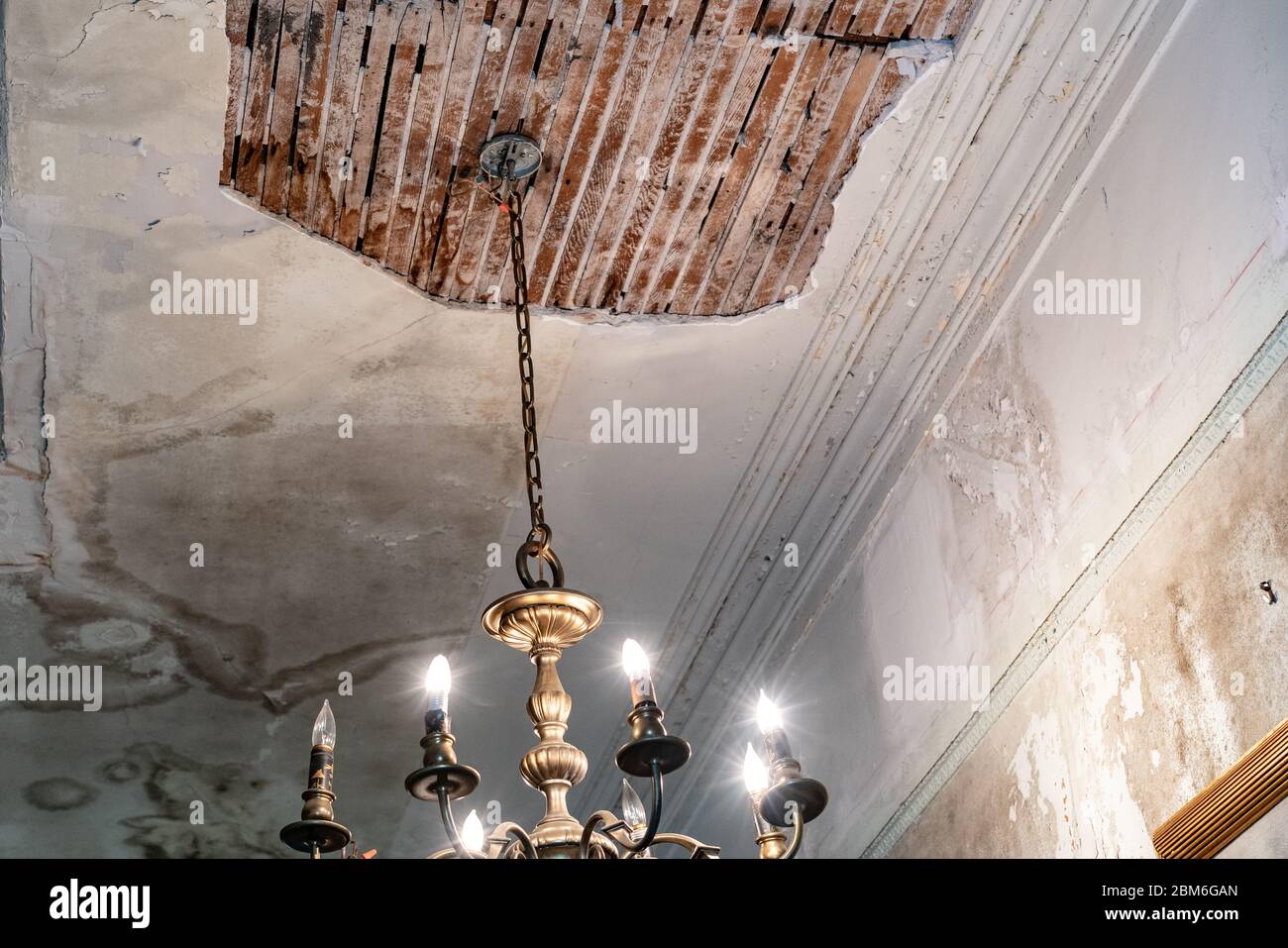 A chandelier illuminates a worn ceiling with a layer of paint peeled ...
