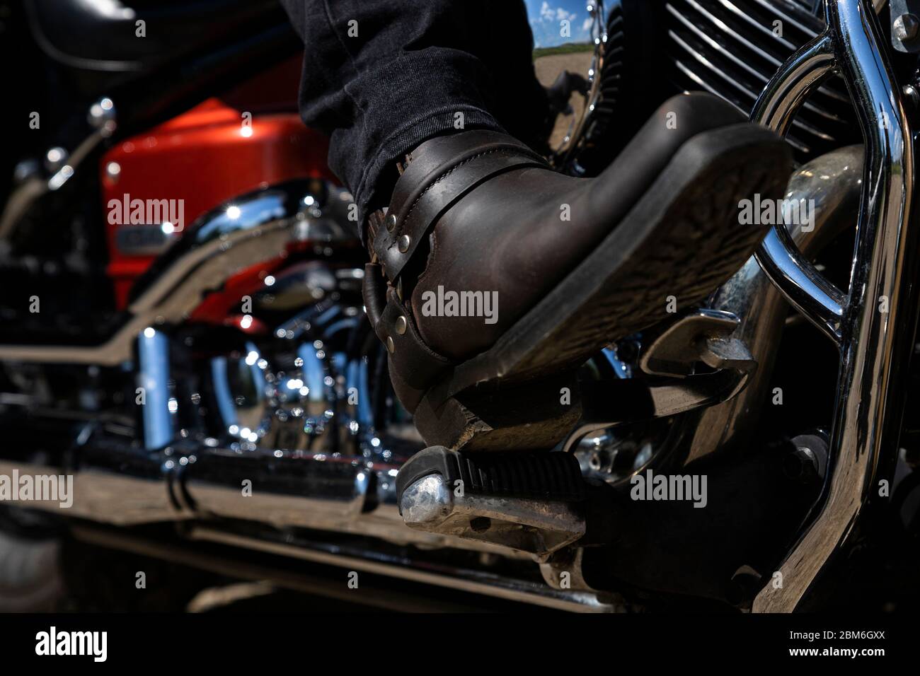 Biker riding a motorcycle. Bottom view of the legs in leather cowboy ...
