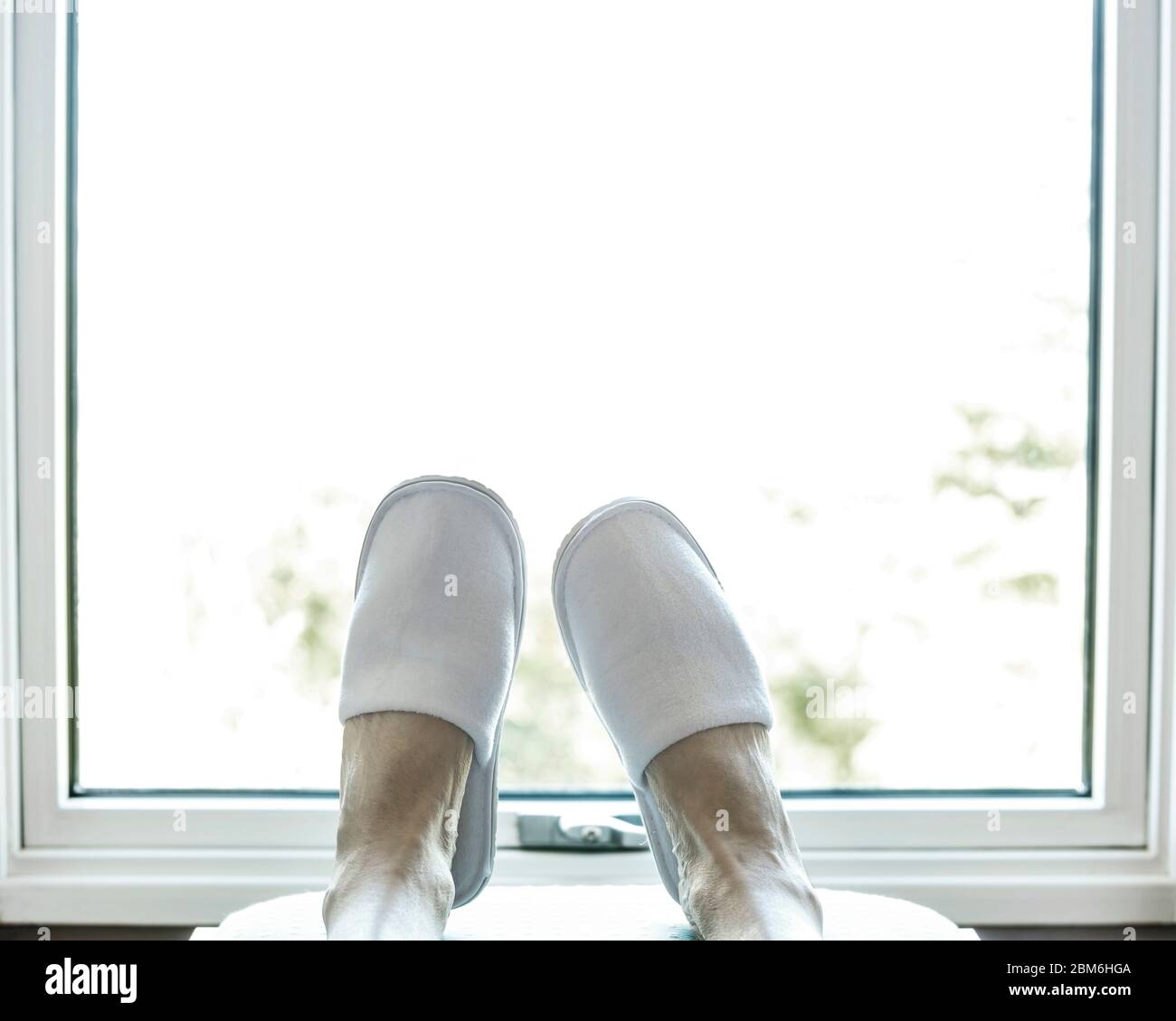 Pair of feet wearing hotel slippers on stool in front of brightly lit ...