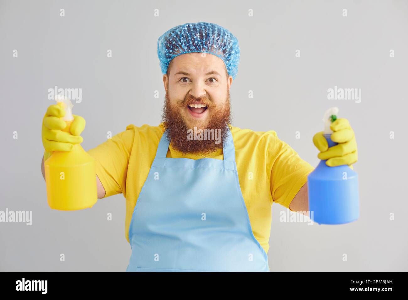 Funny fat man with a beard in an apron cleans up on a gray background ...