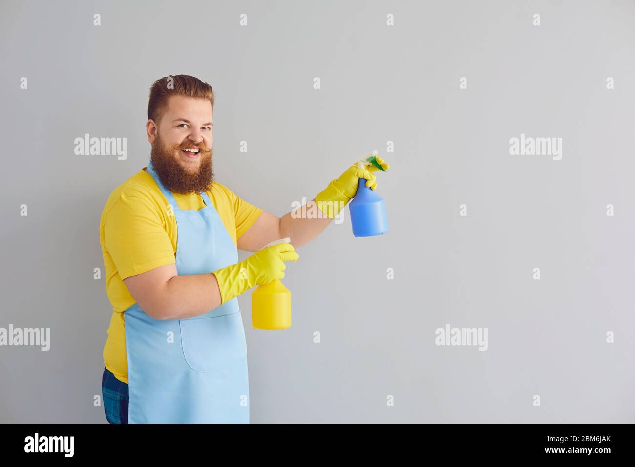 Funny fat man with a beard in an apron washing cleans up on a gray ...