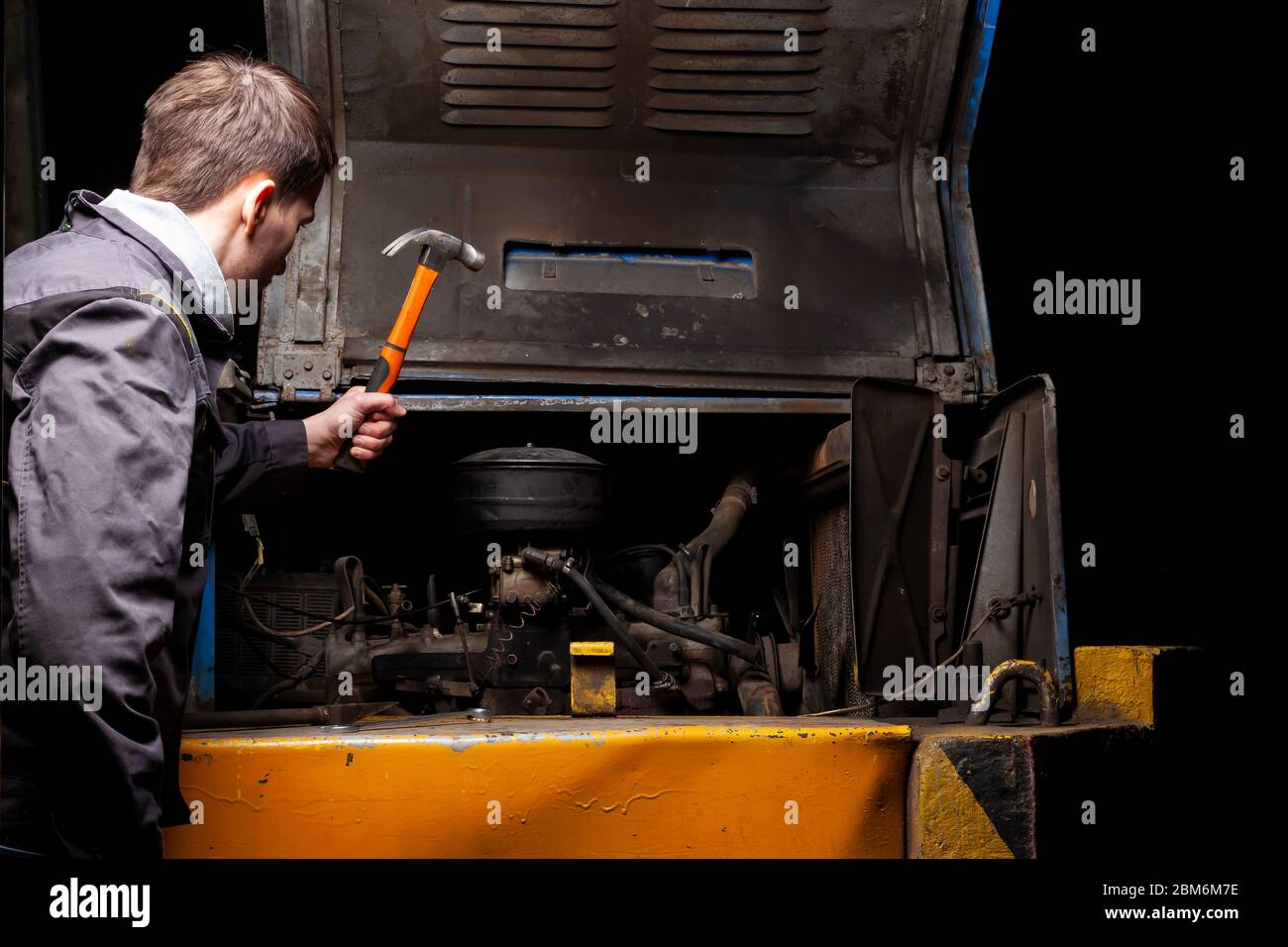 An angry male mechanic is repairing the engine of an old truck with an ...