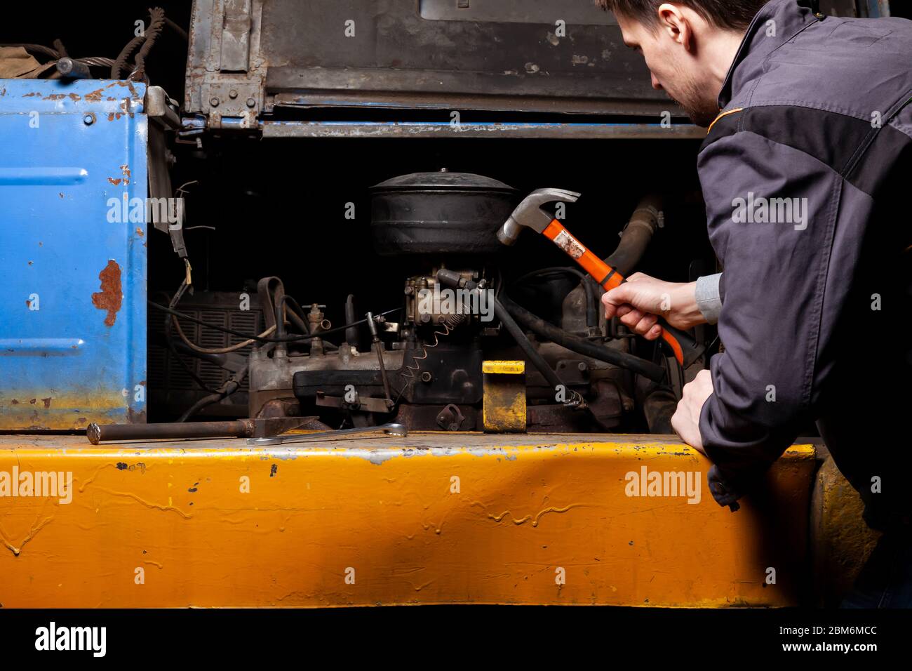 An angry male mechanic is repairing the engine of an old truck with an ...