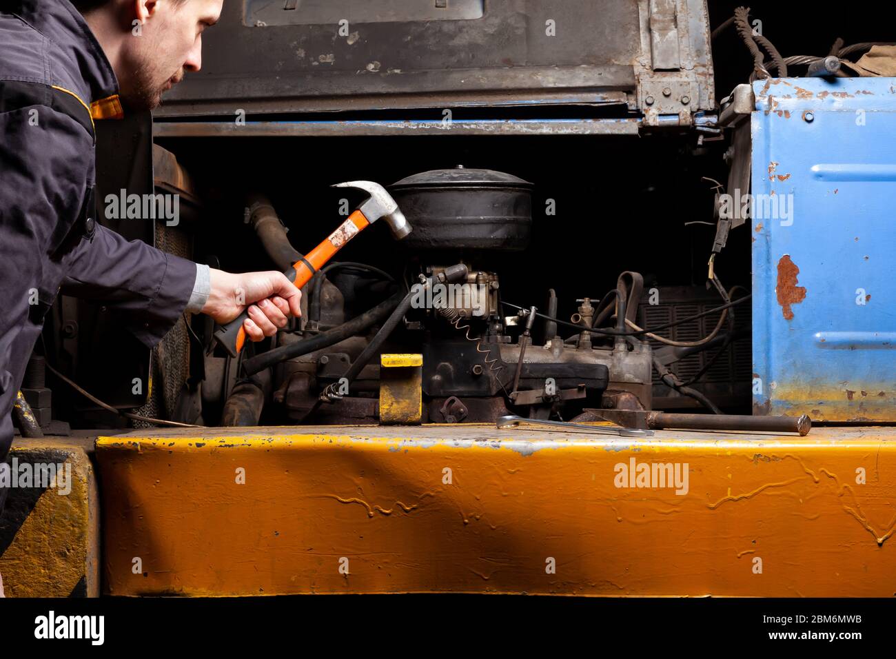 An angry male mechanic is repairing the engine of an old truck with an ...