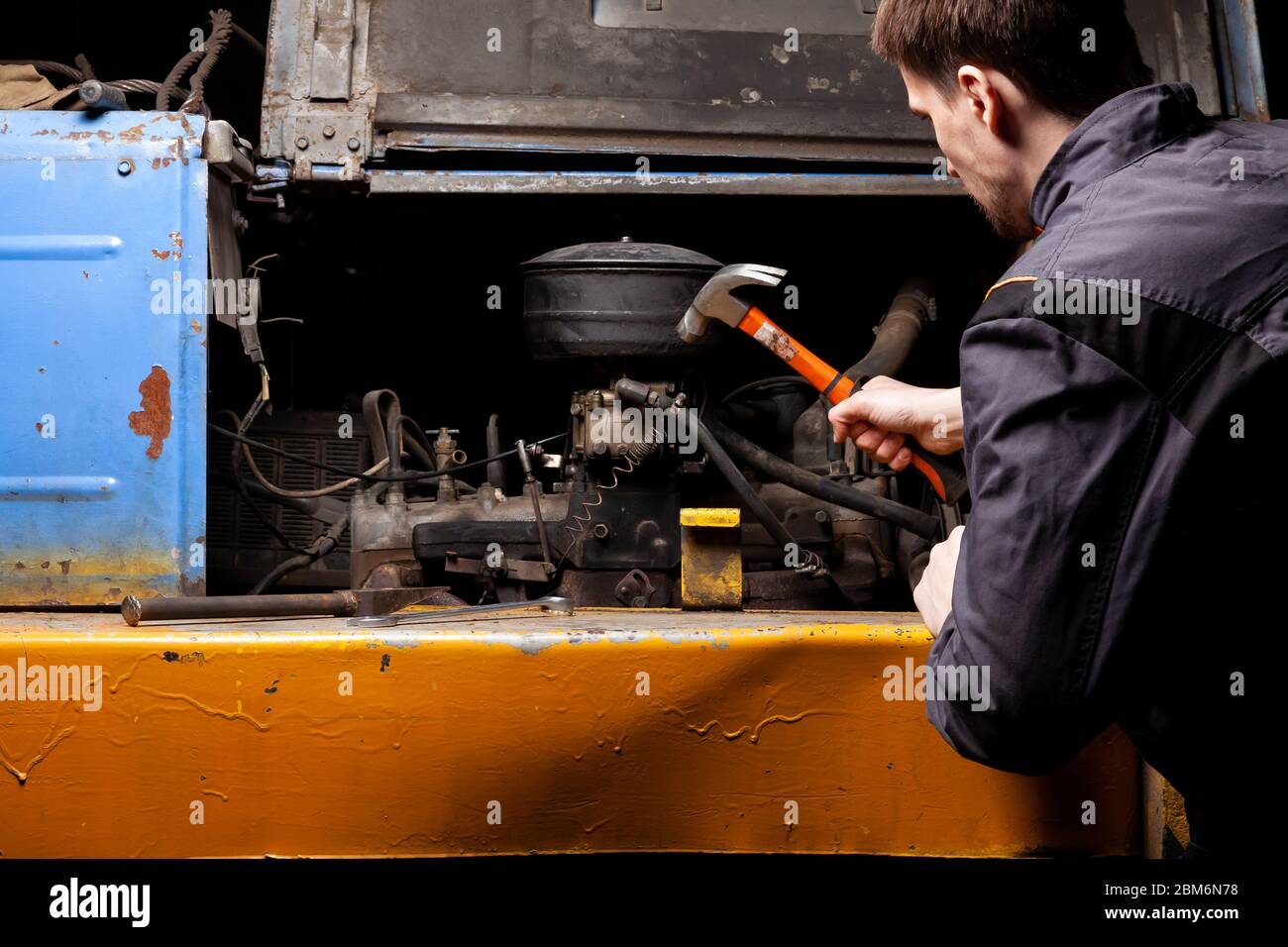 An angry male mechanic is repairing the engine of an old truck with an ...