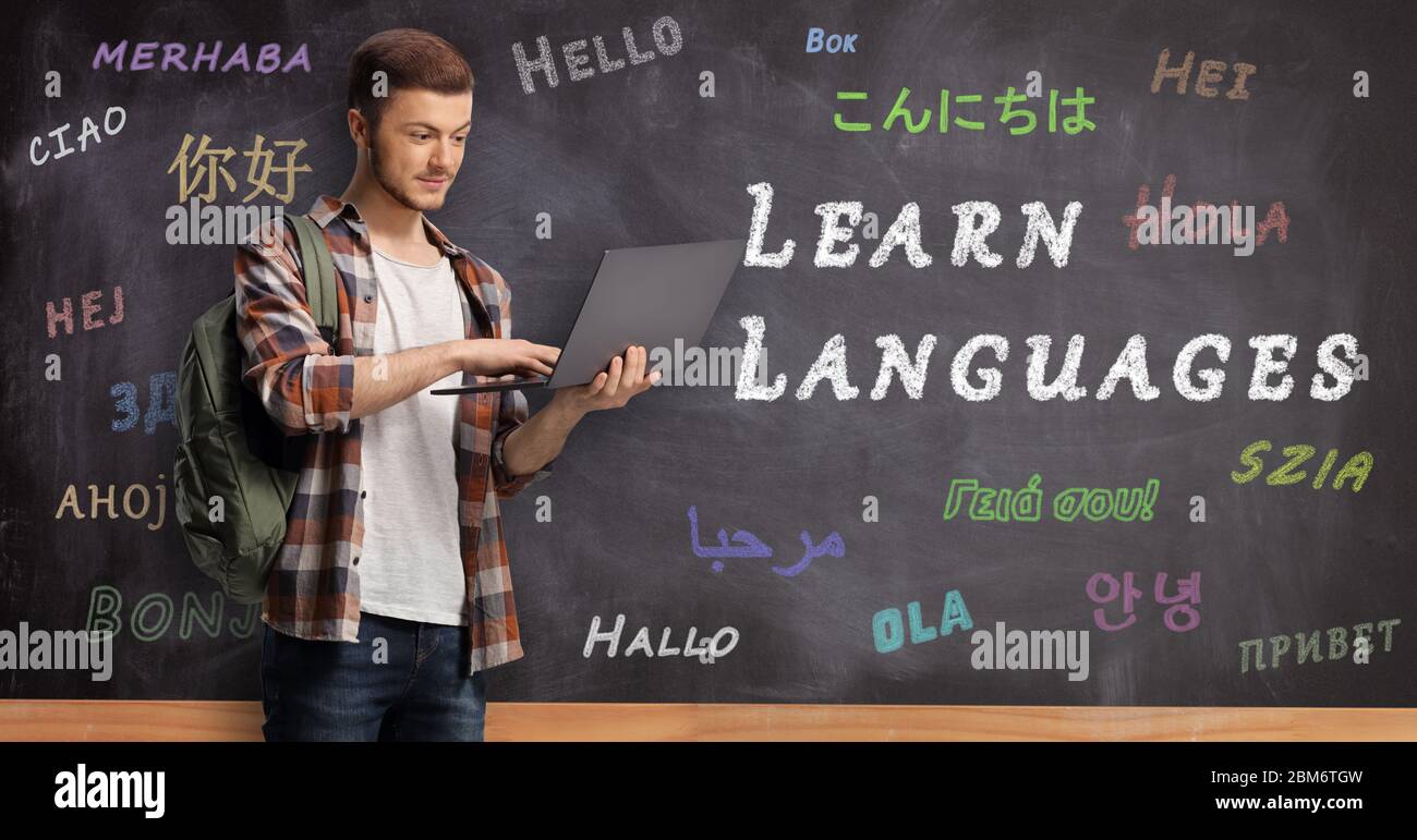 Male student with a laptop and standing in front of a blackboard with ...