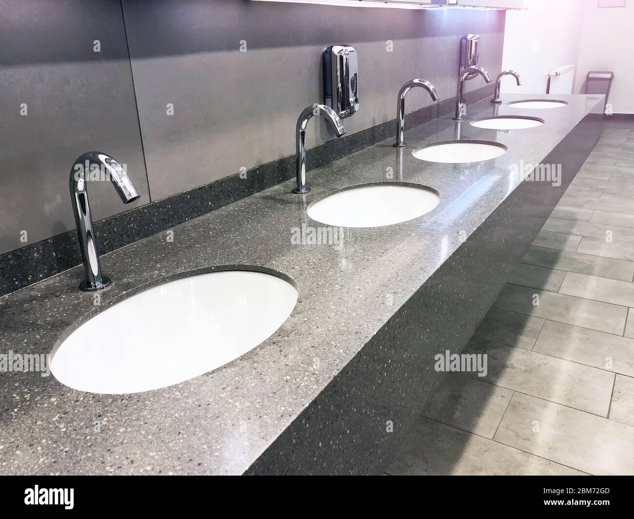 A row of washstands with a water tap and a soap dispenser in a public ...