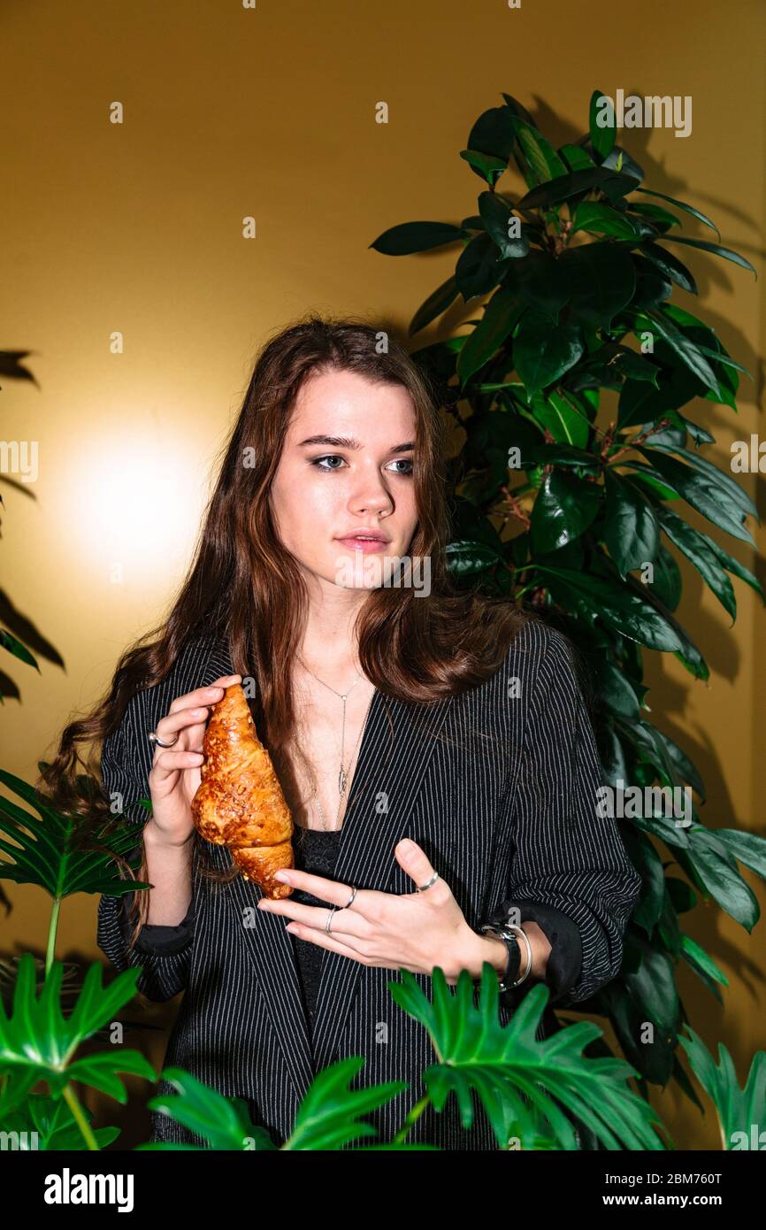 Girl with croissant stands near plant in studio Stock Photo - Alamy