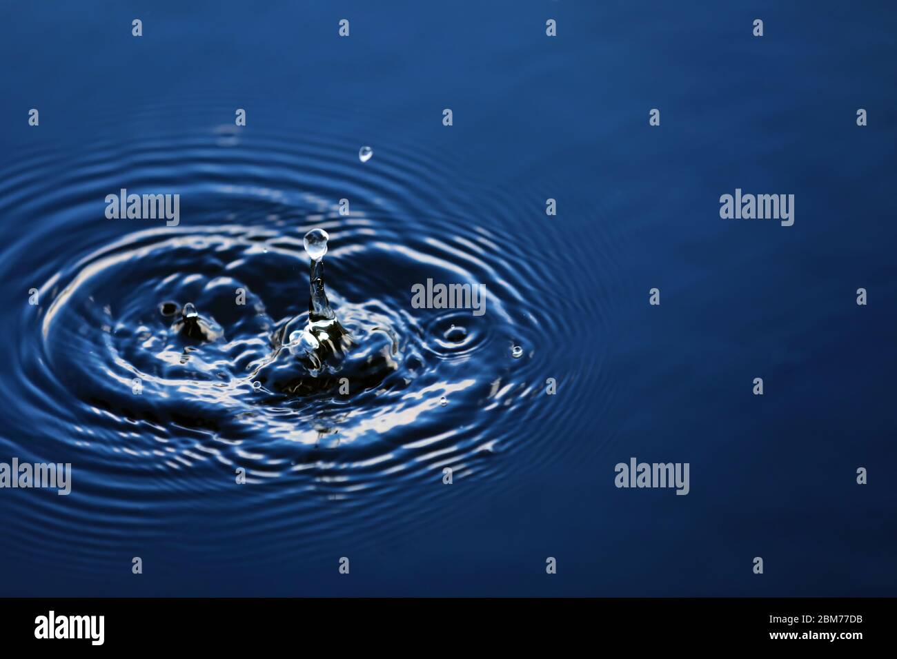A drop of water falls into the water, making a perfect splash of drops ...